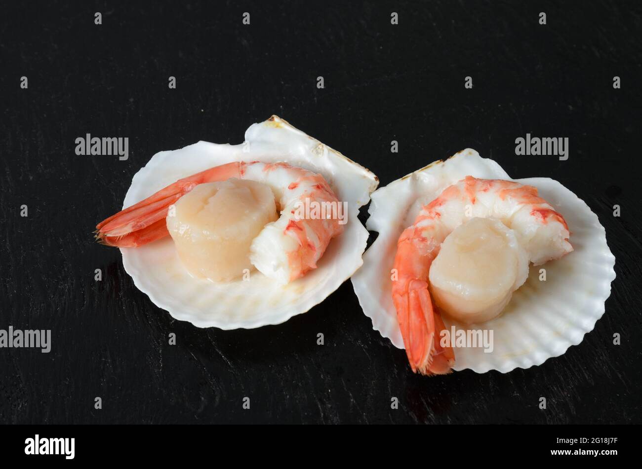 Raw scallop with a boiled shrimp tail in a shell on a black wooden ...