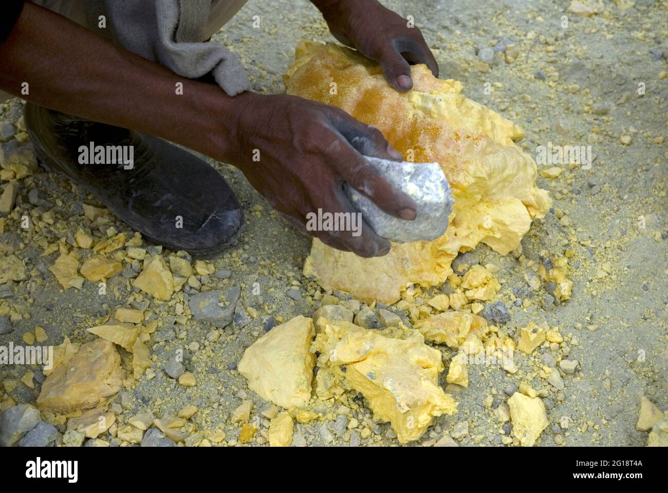 A miner breaks the sulphur chunks into pieces with a stone inside Kawah ...