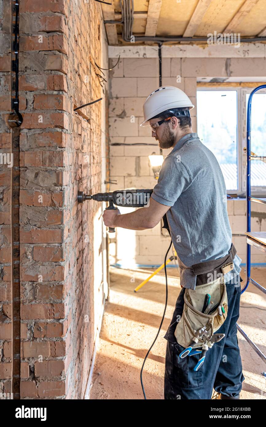 Handyman at a construction site in the process of drilling a wall with ...