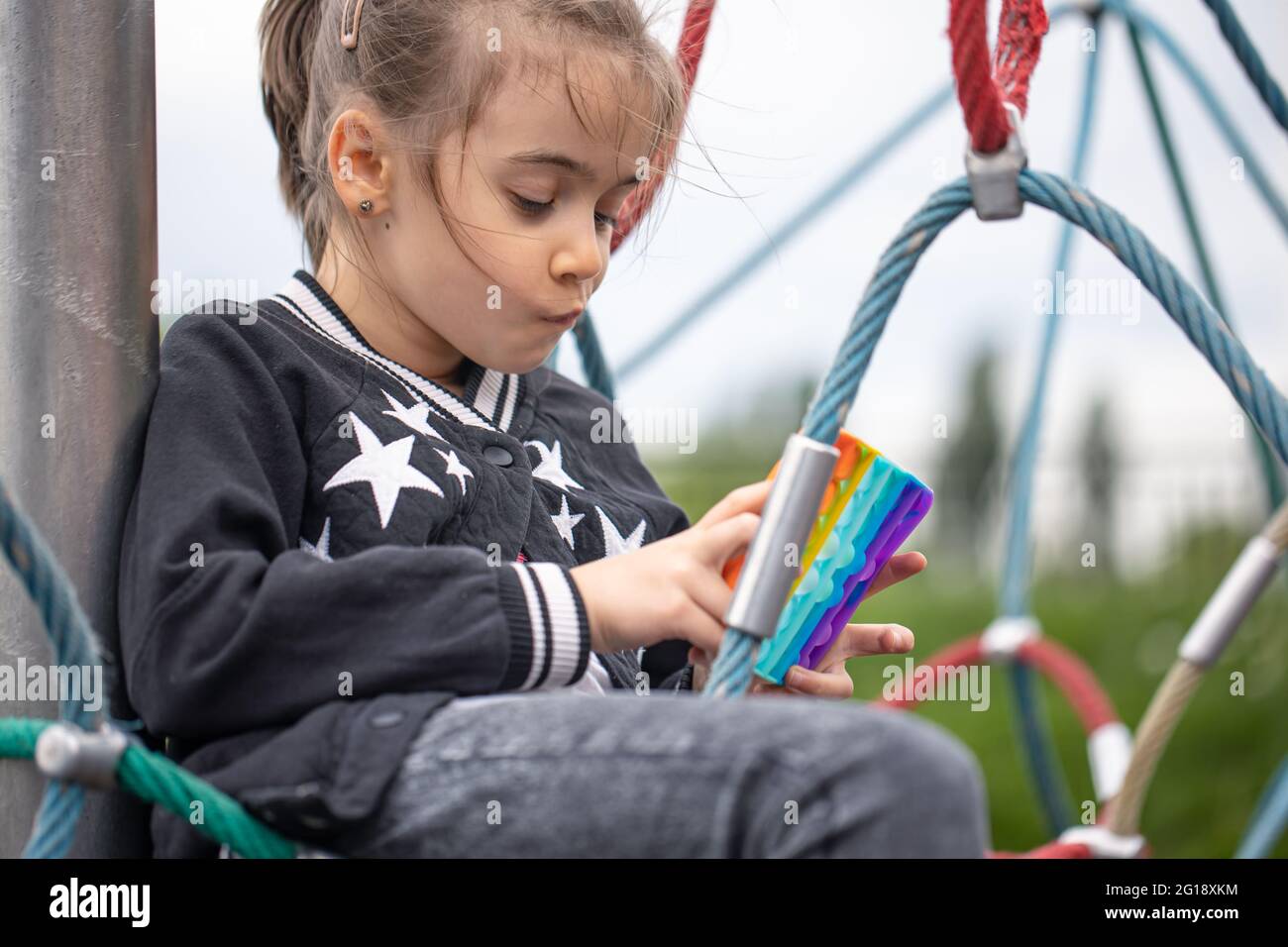 A little cheerful girl plays with a popular colorful toy antistress pop ...