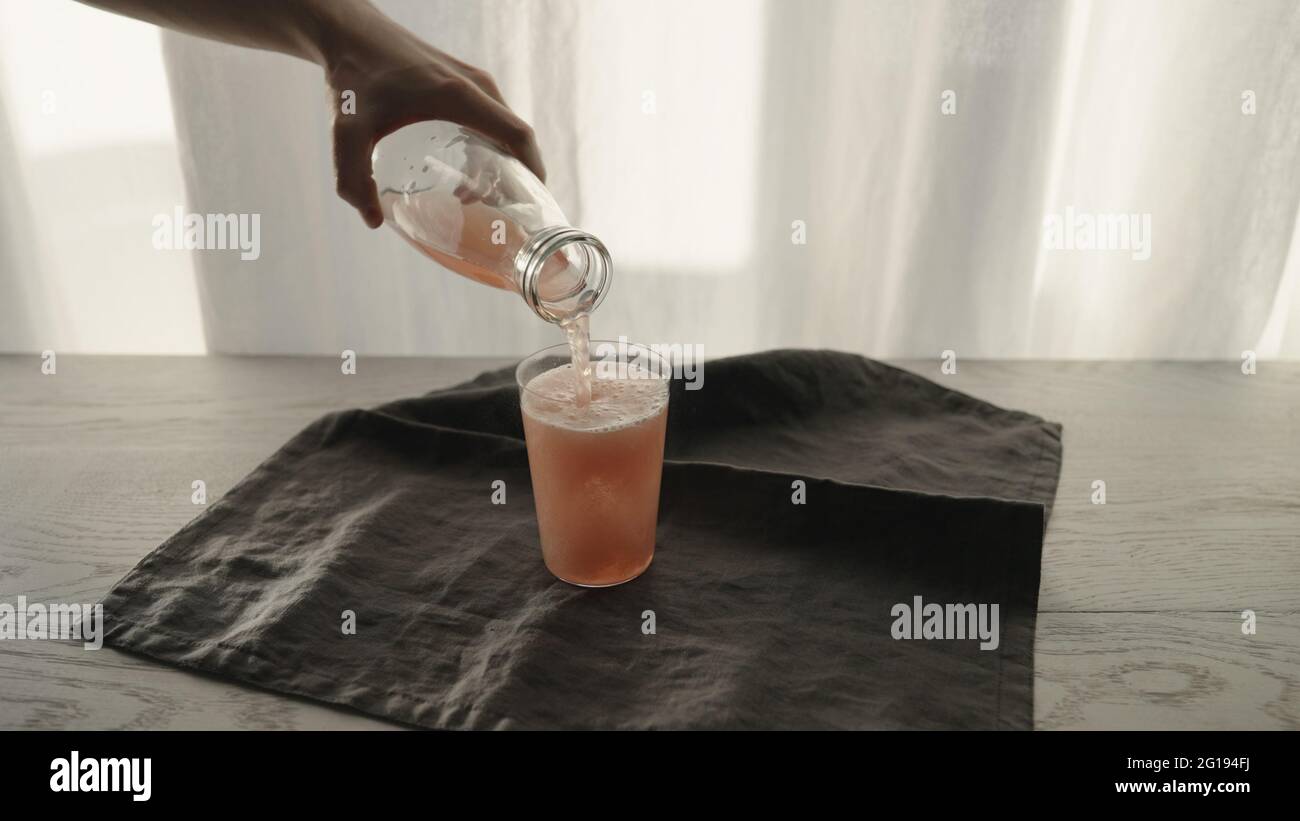 man serving pink sparkling drink into tumbler glass with ice chunk ...