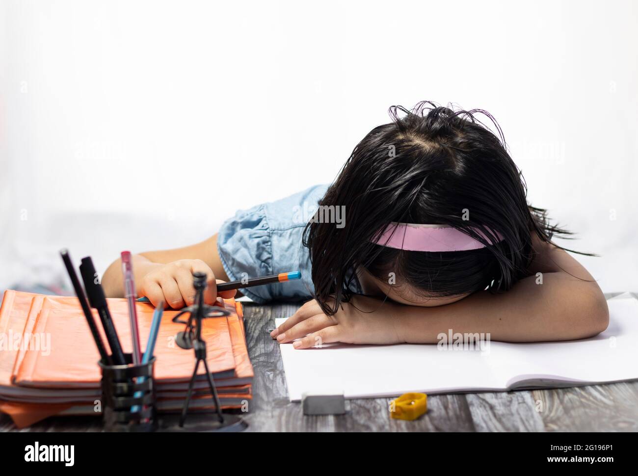 An Indian girl child resting head on table during studying on white ...