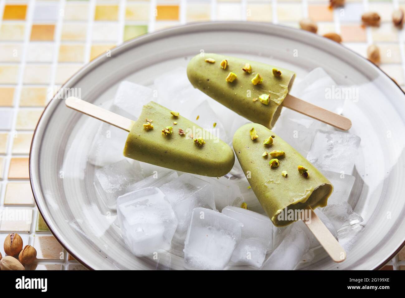 Frozen homemade pistachio popsicle in bowl of ice on mosaic tile table ...