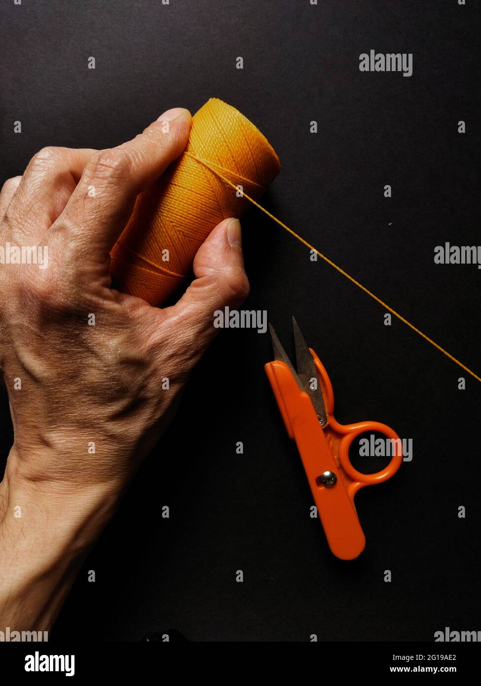 A vertical top view of a person's hand holding a yellow thread with ...