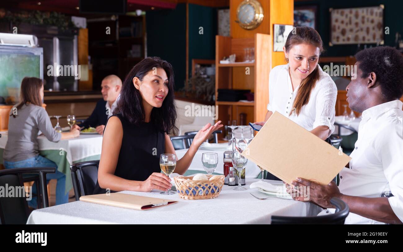 Polite young waitress helping with menu to African American Stock Photo ...