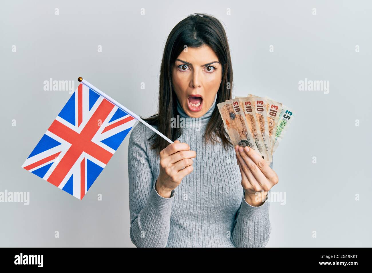 Young hispanic woman holding united kingdom flag and pounds banknotes ...