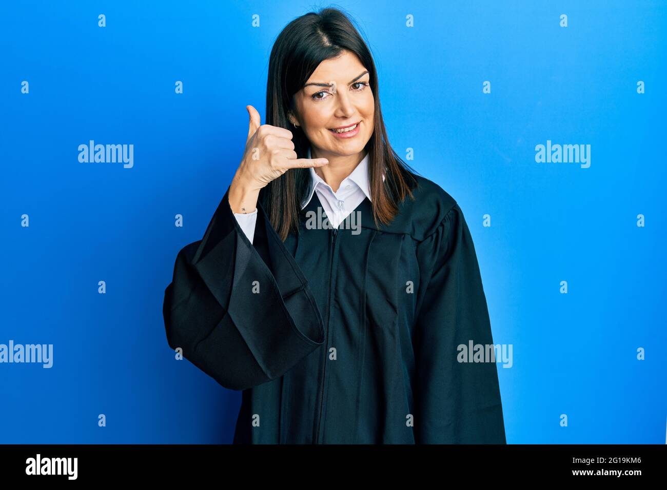 Young hispanic woman wearing judge uniform smiling doing phone gesture ...