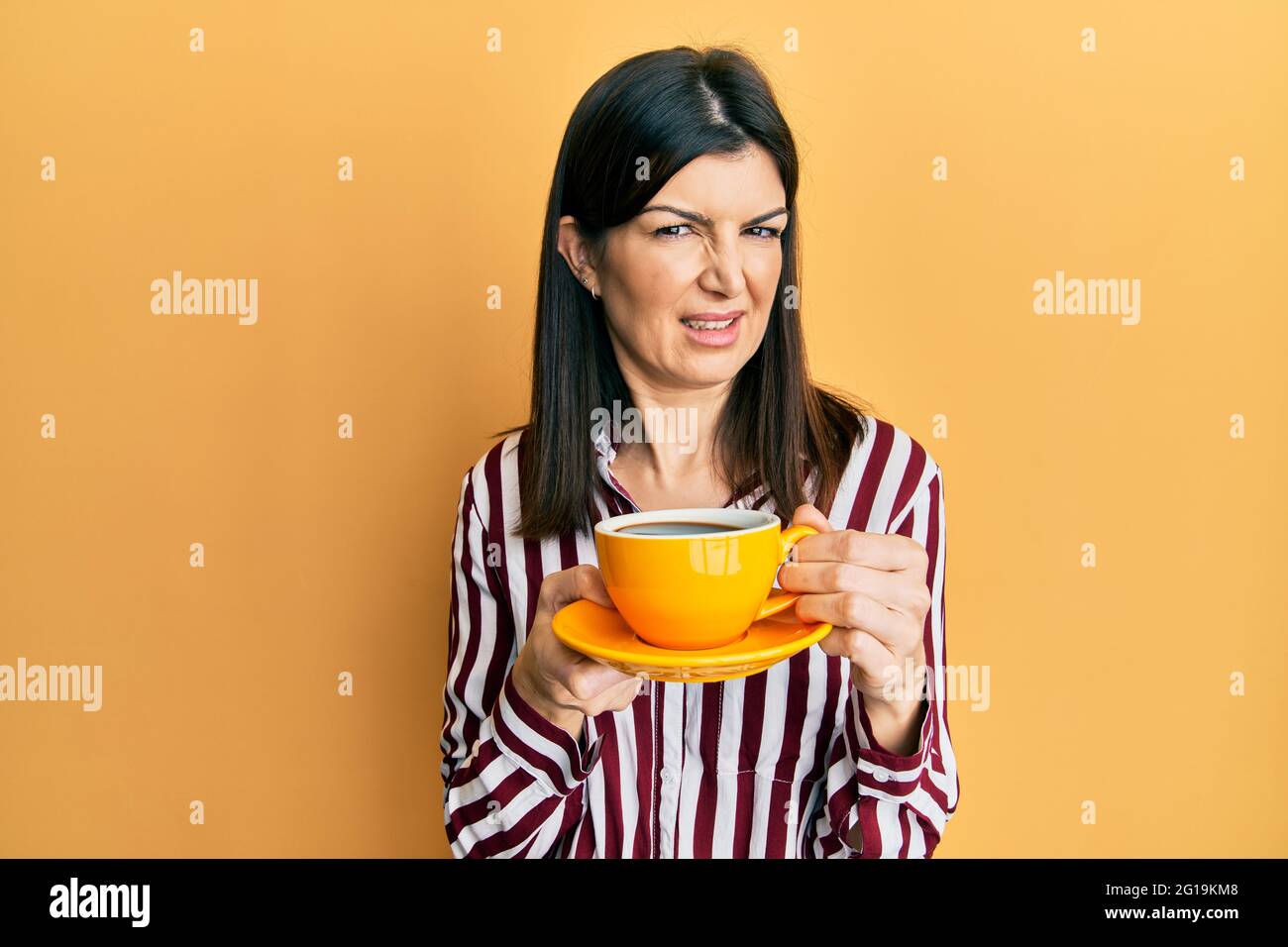Young hispanic woman drinking a cup of coffee clueless and confused ...