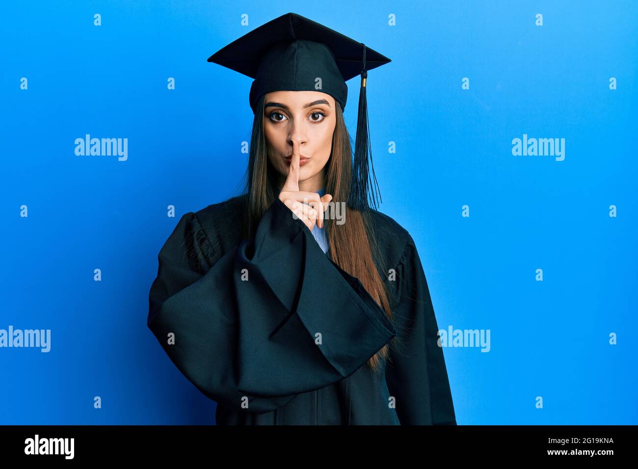 Beautiful brunette young woman wearing graduation cap and ceremony robe ...