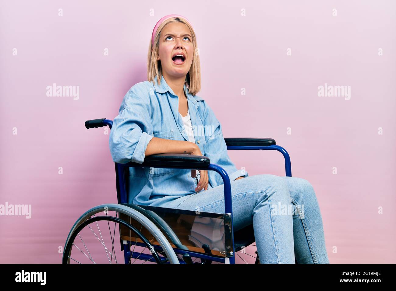 Beautiful blonde woman sitting on wheelchair angry and mad screaming ...