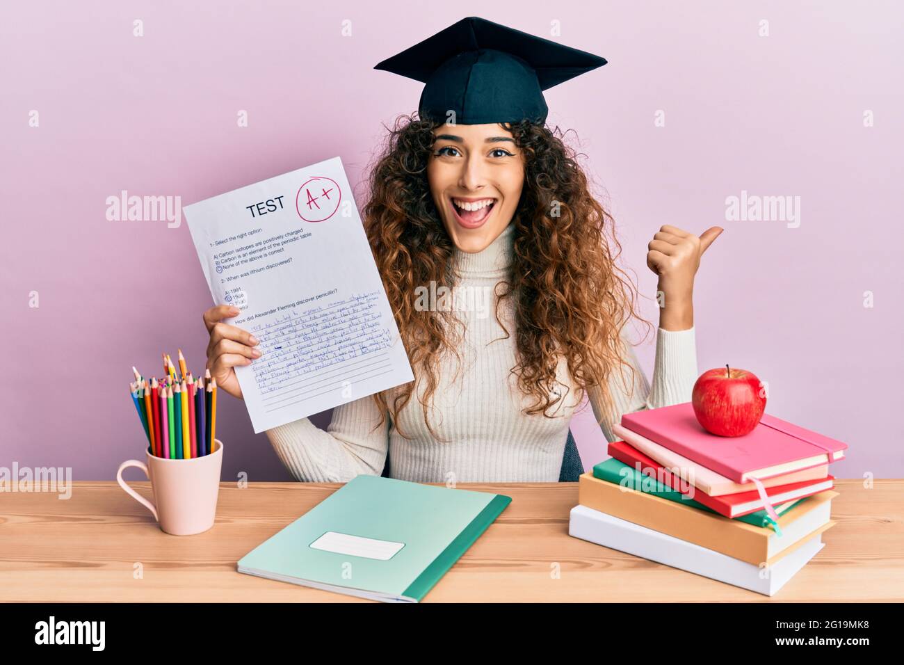 Young hispanic girl wearing graduated hat holding passed test pointing ...