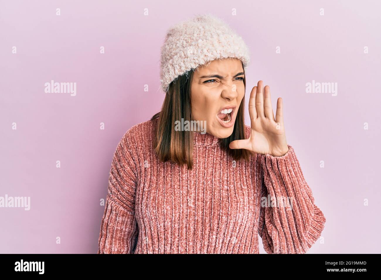 Young beautiful woman wearing wool sweater and winter hat shouting and ...
