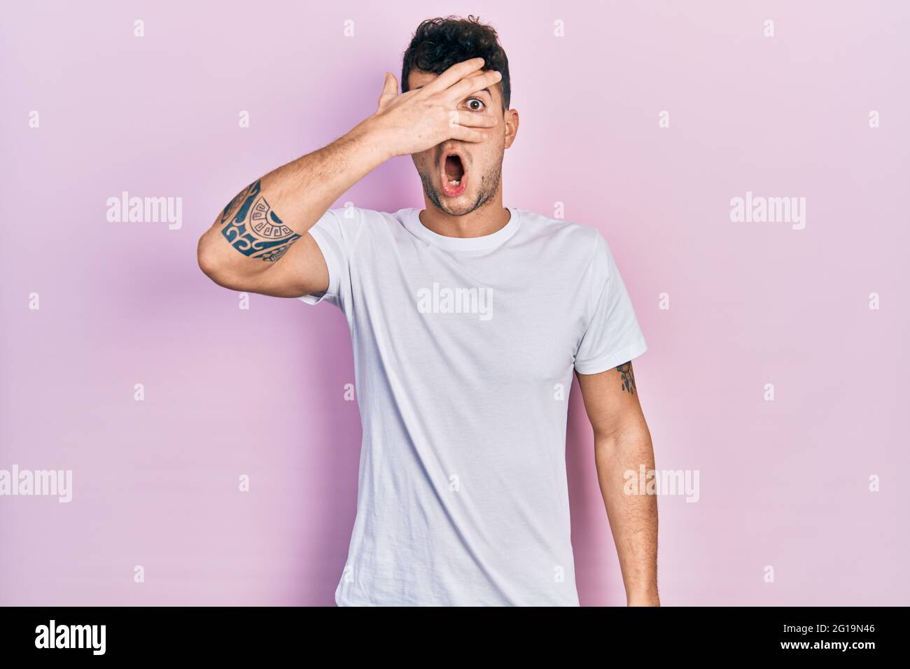 Young hispanic man wearing casual white t shirt peeking in shock ...