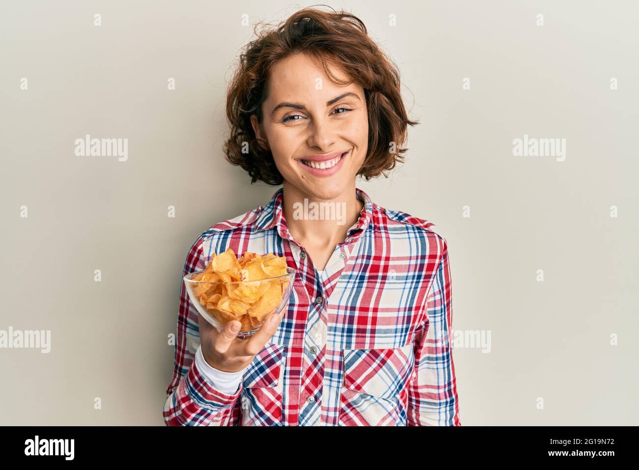 Young brunette woman holding potato chips looking positive and happy ...