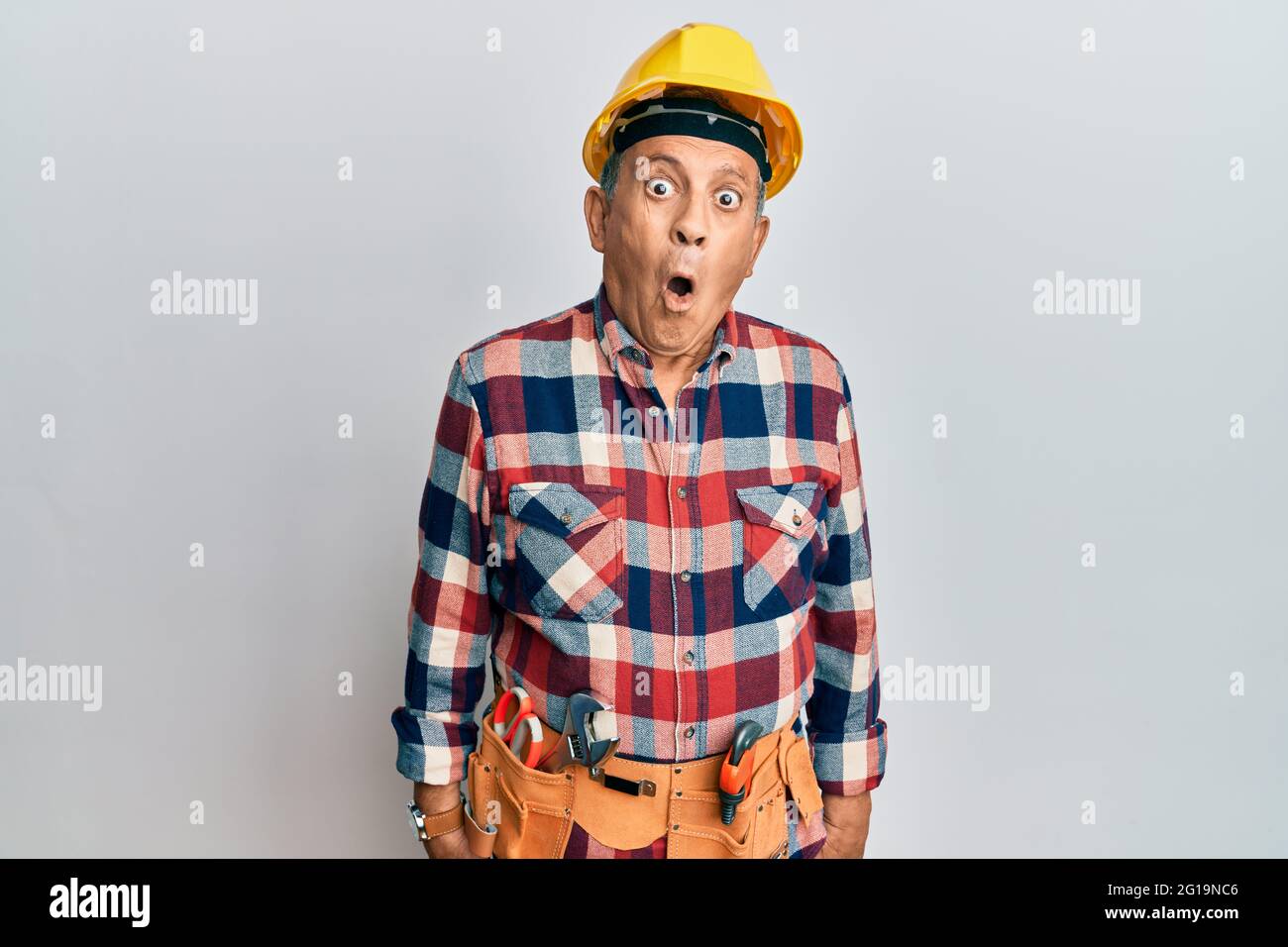 Senior hispanic man wearing handyman uniform afraid and shocked with ...
