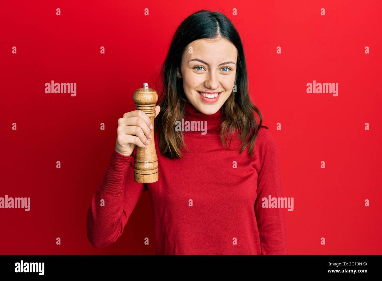 Young brunette woman black pepper grinder looking positive and happy ...