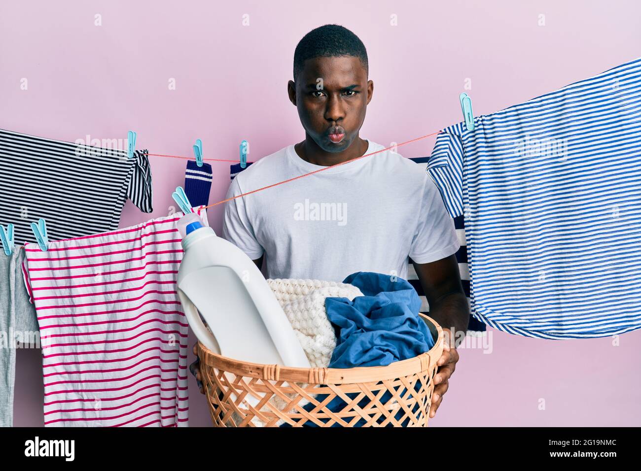 Young african american man holding laundry basket making fish face with ...