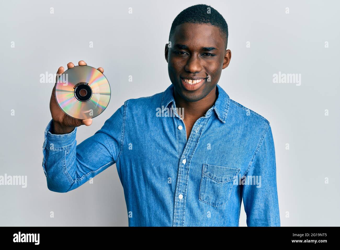 Young african american man holding compact disc looking positive and ...