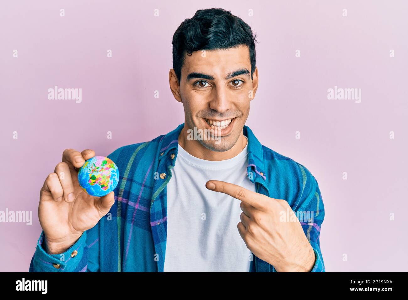 Handsome hispanic man holding small world ball smiling happy pointing ...
