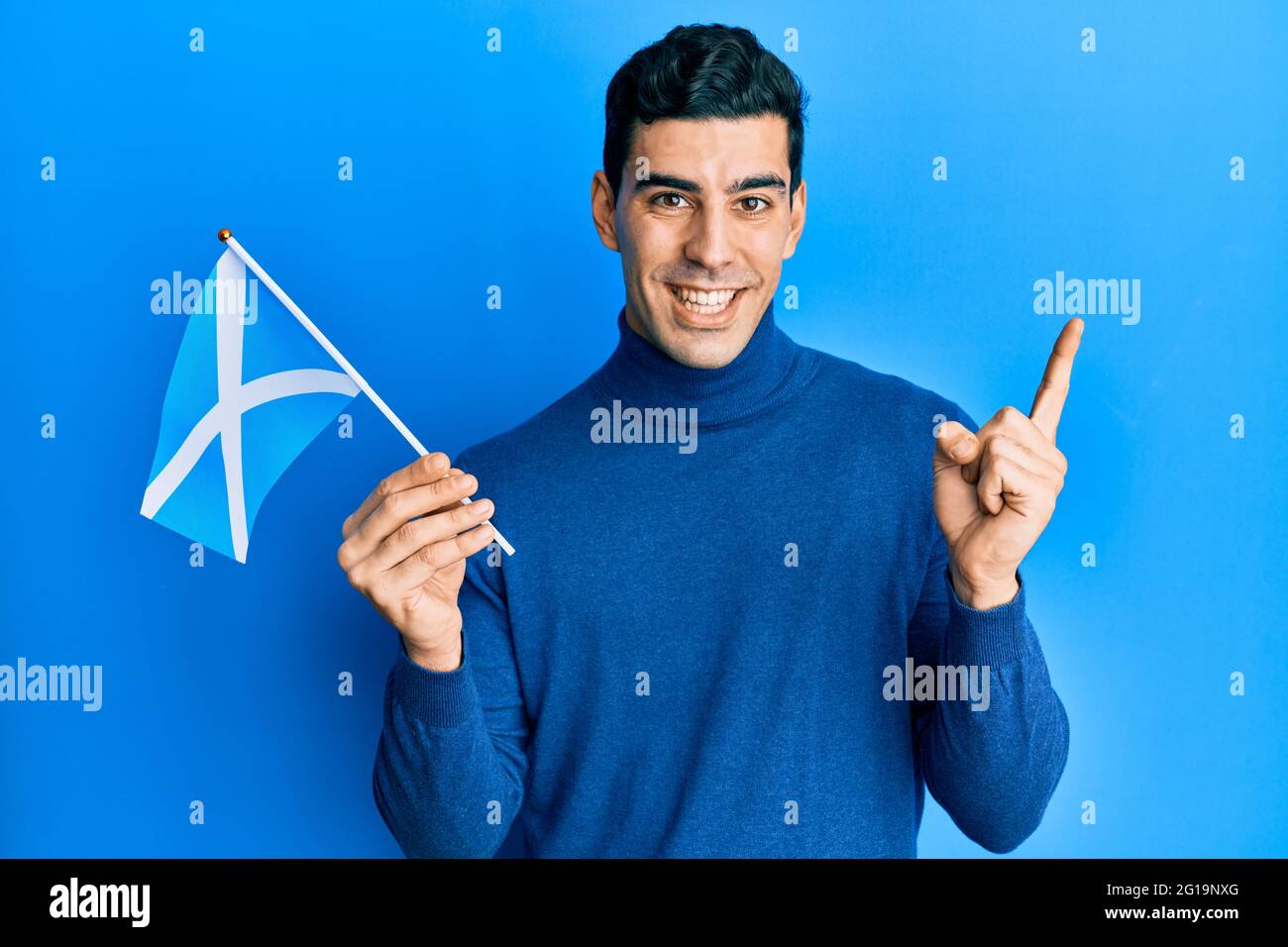 Handsome hispanic man holding scotland flag smiling happy pointing with ...
