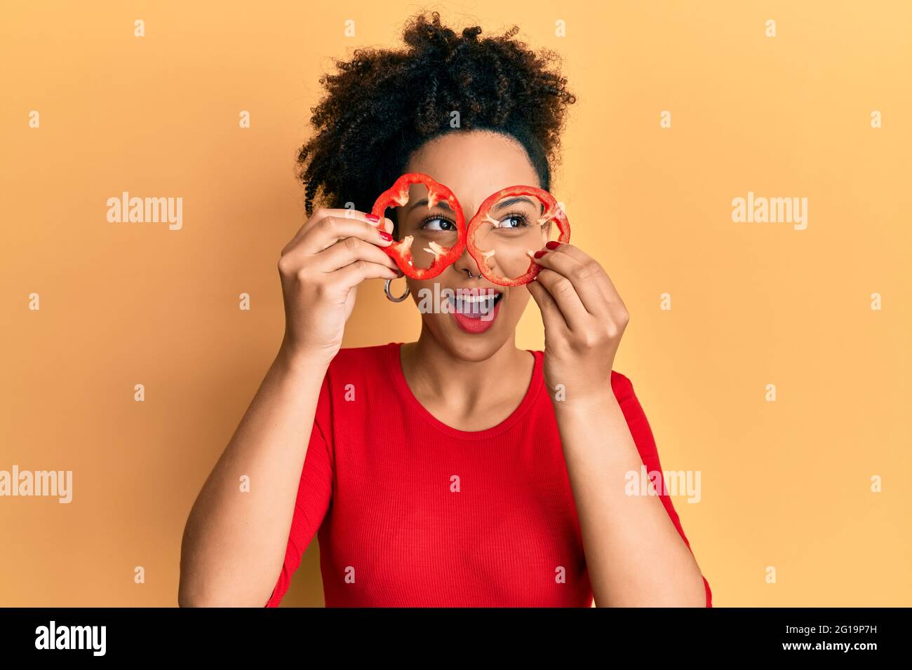 Young african american girl holding red pepper as a glasses angry and ...
