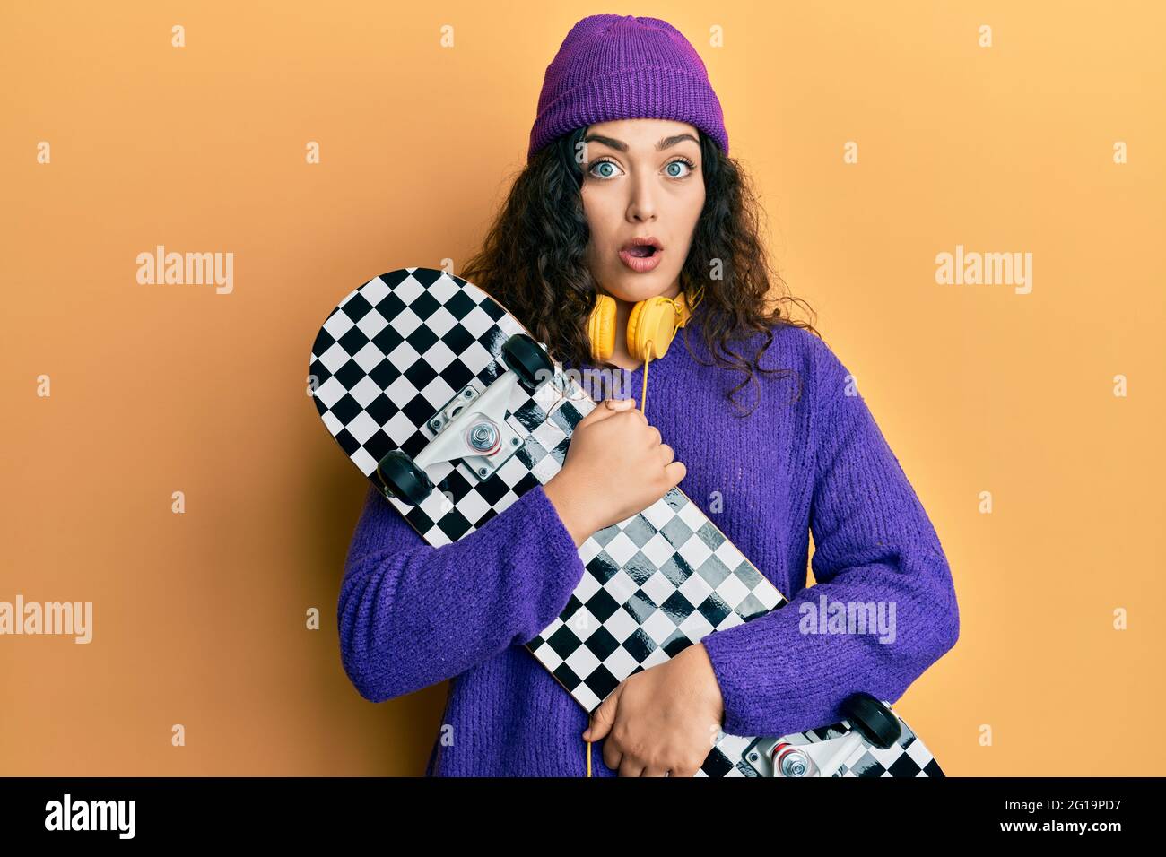 Young brunette woman with curly hair holding skate afraid and shocked ...