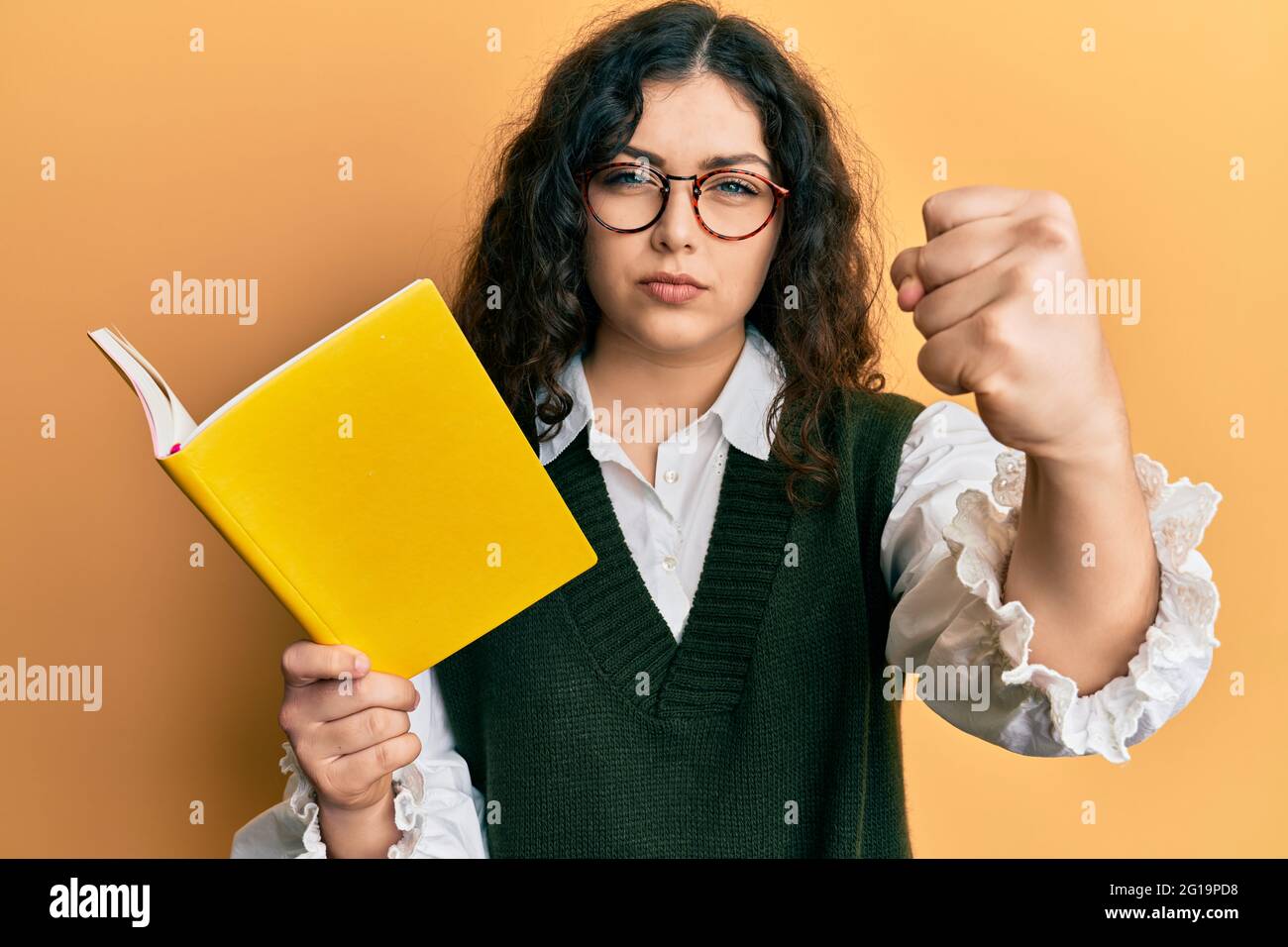 Young brunette woman with curly hair reading a book wearing glasses ...