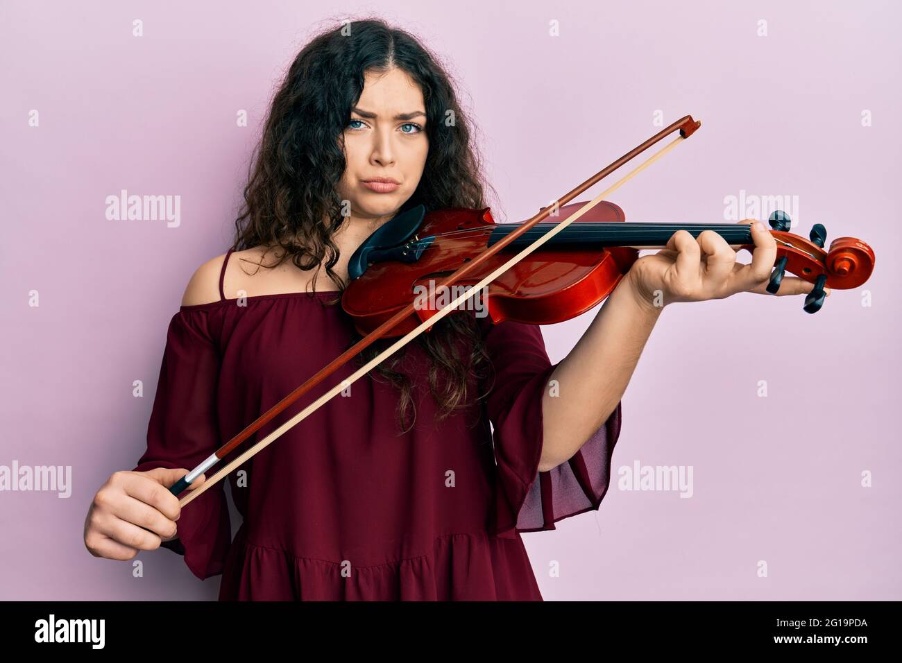Young brunette musician woman with curly hair playing violin depressed ...