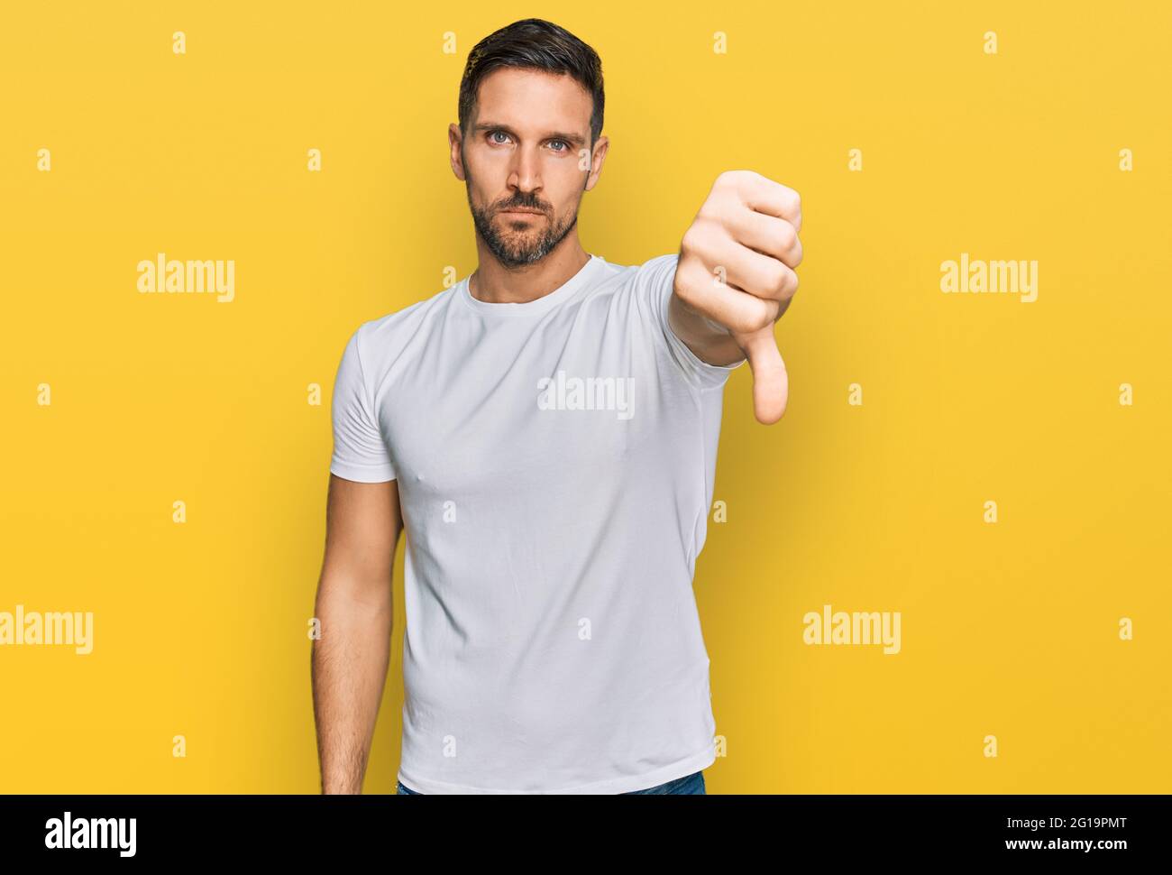 Handsome man with beard wearing casual white t shirt looking unhappy ...