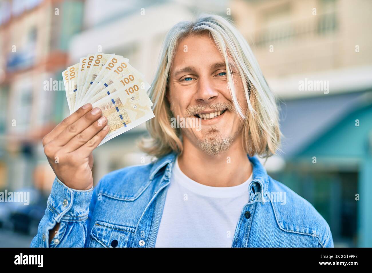 Young blond scandinavian man smiling happy holding danmark 100 kroner ...