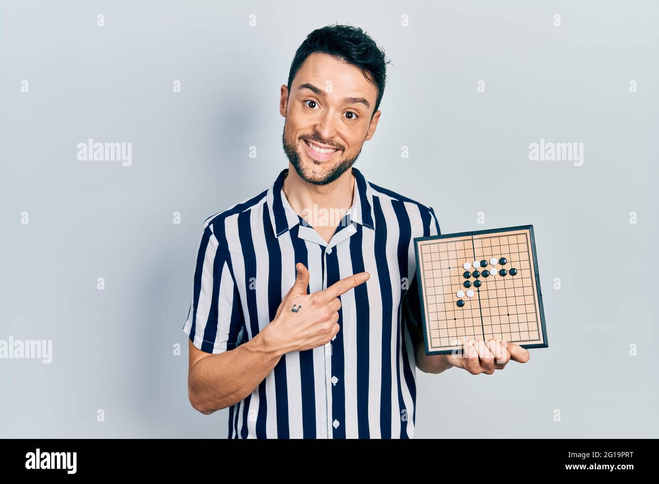 Young hispanic man holding asian go game board smiling happy pointing ...