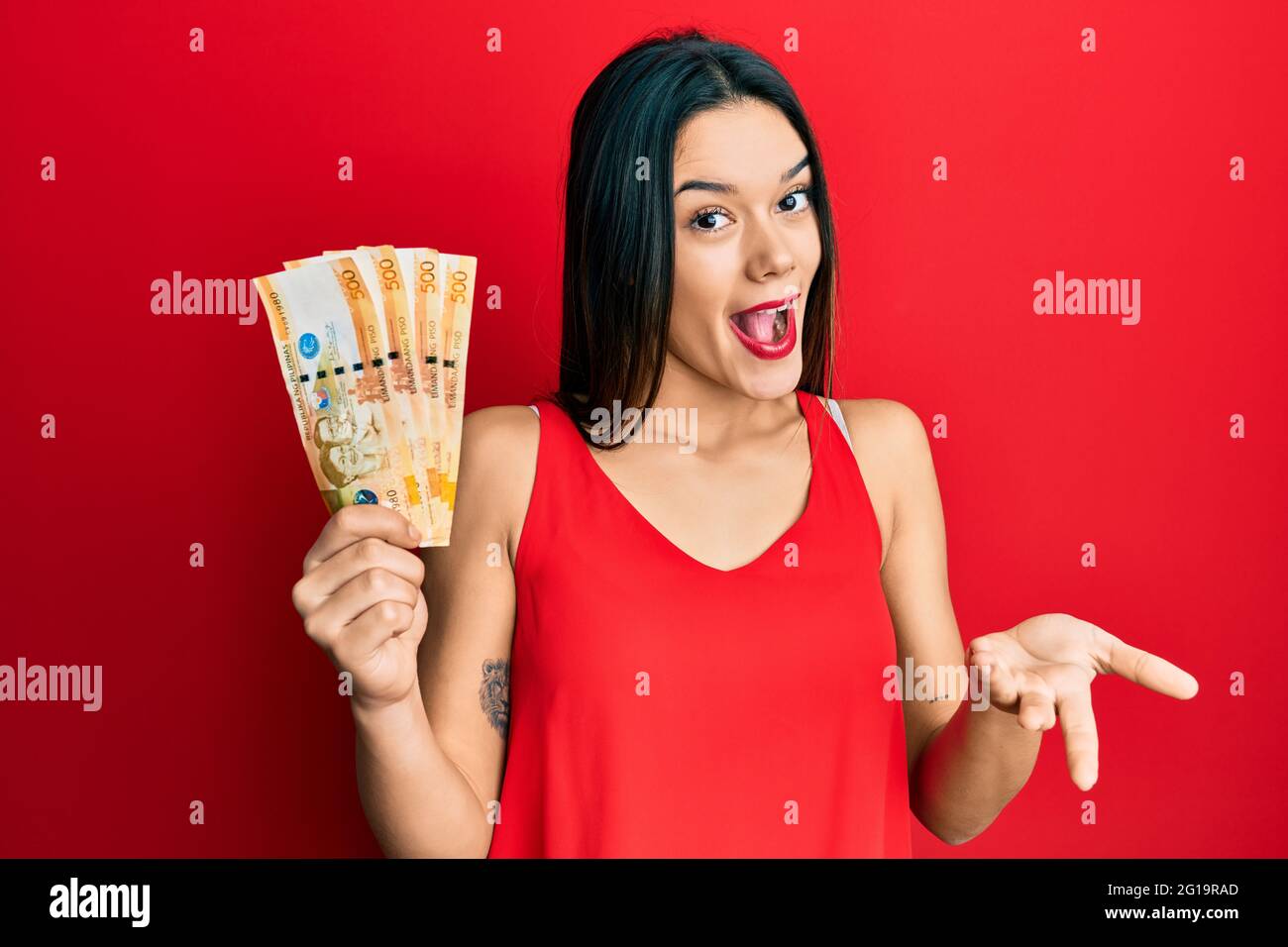 Young hispanic girl holding 500 philippine peso banknotes celebrating ...
