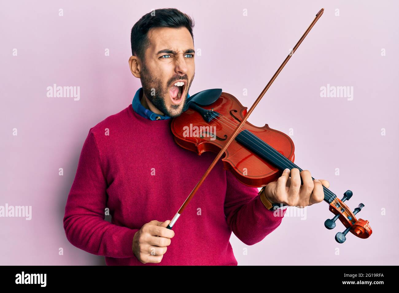 Young hispanic musician man playing violin angry and mad screaming ...