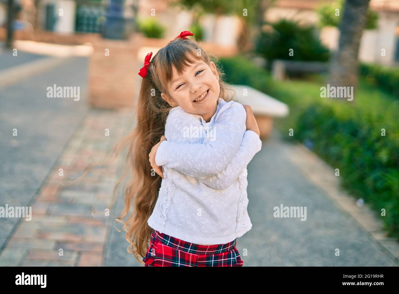 Adorable caucasian child girl smiling happy hugging himself at the city ...