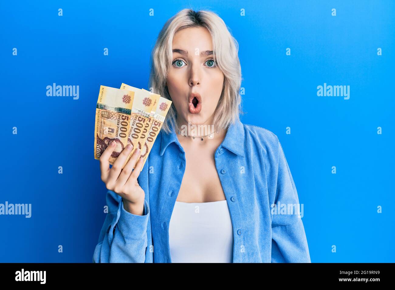Young blonde girl holding hungarian forint banknotes scared and amazed ...