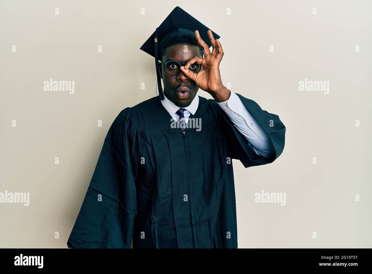 Handsome black man wearing graduation cap and ceremony robe doing ok ...
