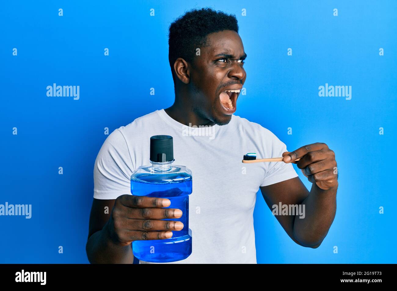 Handsome black man holding mouthwash and toothbrush for fresh breath ...