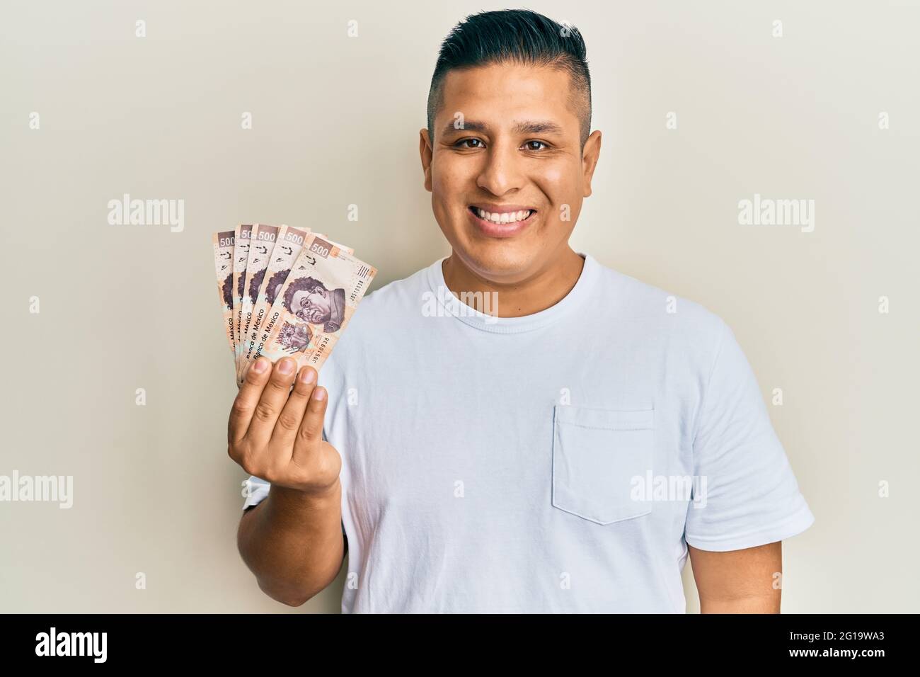 Young latin man holding 500 mexican pesos banknotes looking positive ...