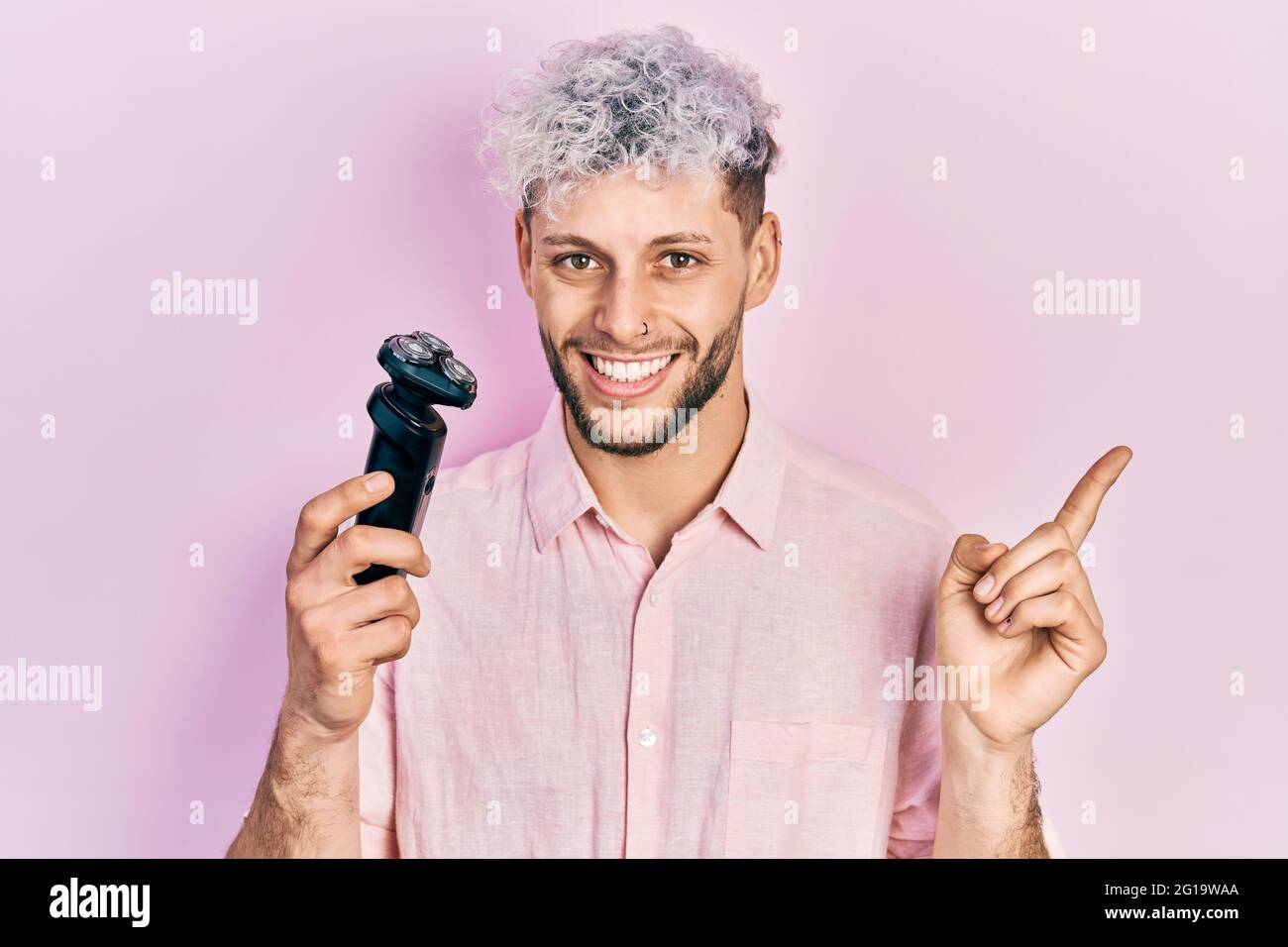 Young hispanic man with modern dyed hair holding electric razor machine ...