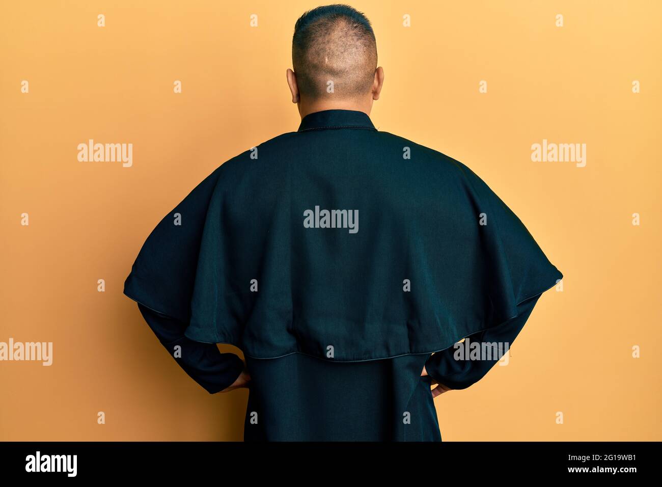 Young latin priest man standing over yellow background standing ...