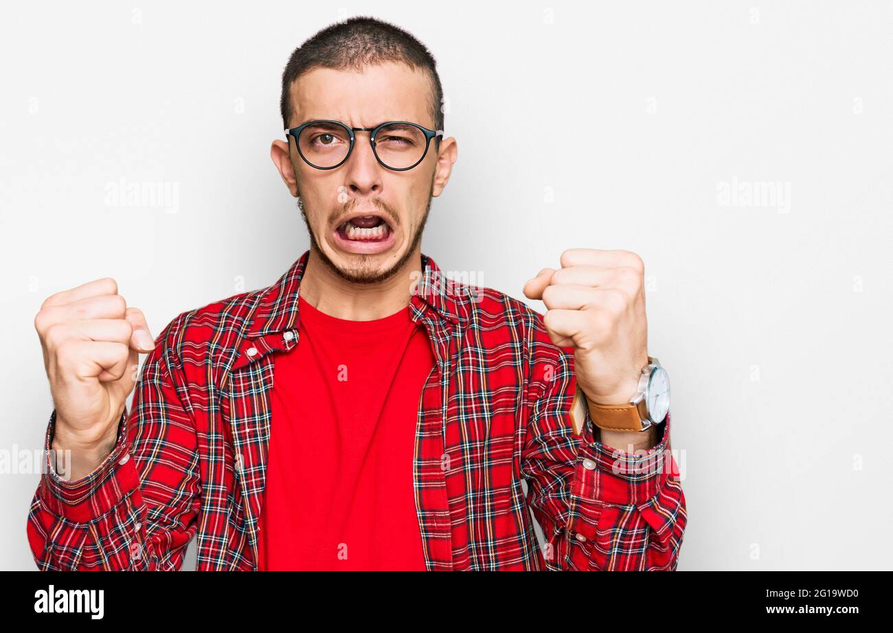Hispanic young man wearing casual clothes angry and mad raising fists ...
