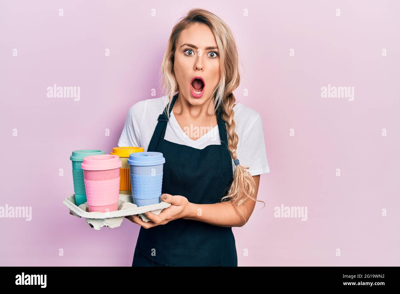 Beautiful young blonde woman wearing waitress apron holding take away ...
