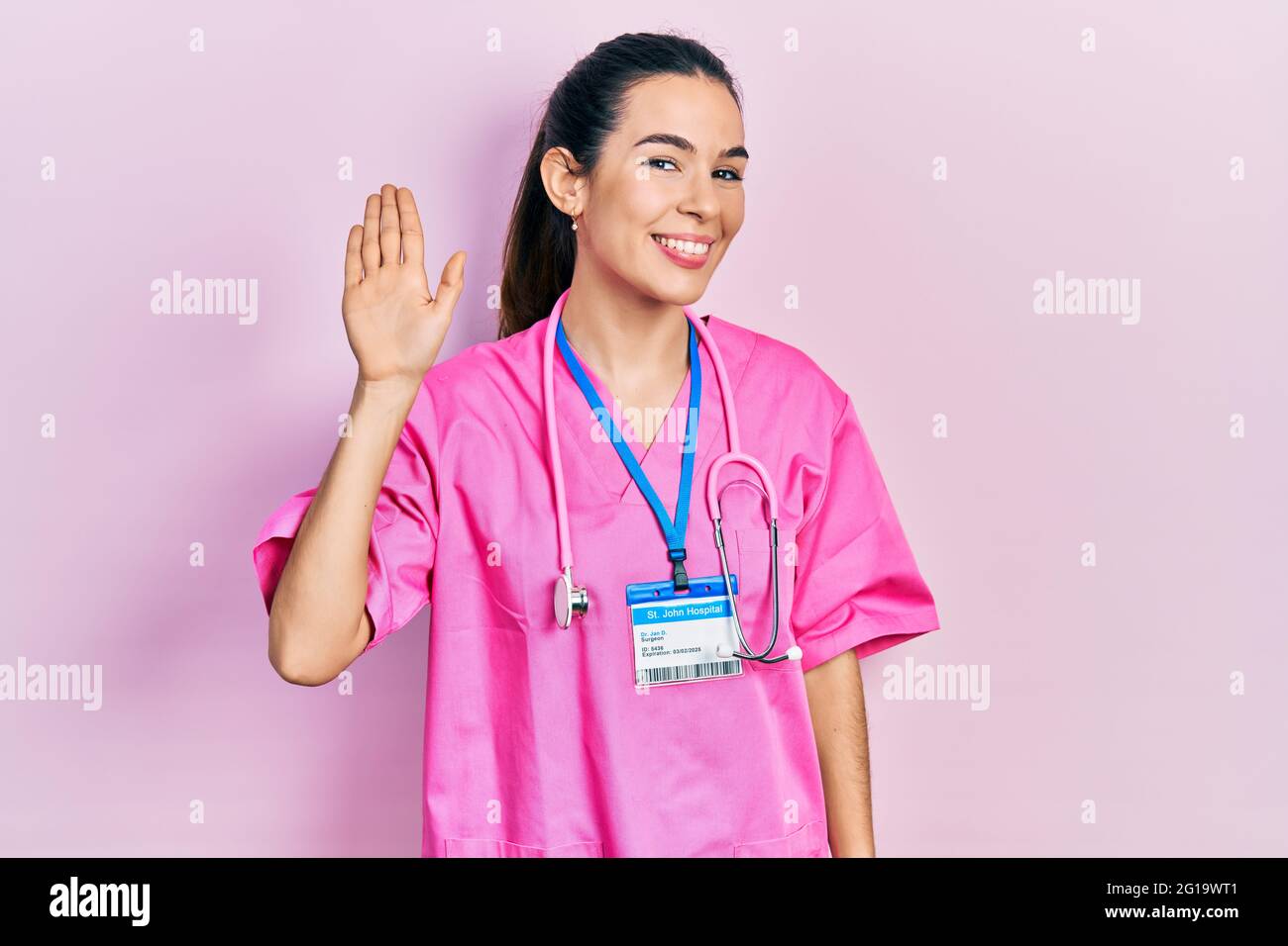 Young brunette woman wearing doctor uniform and stethoscope waiving ...