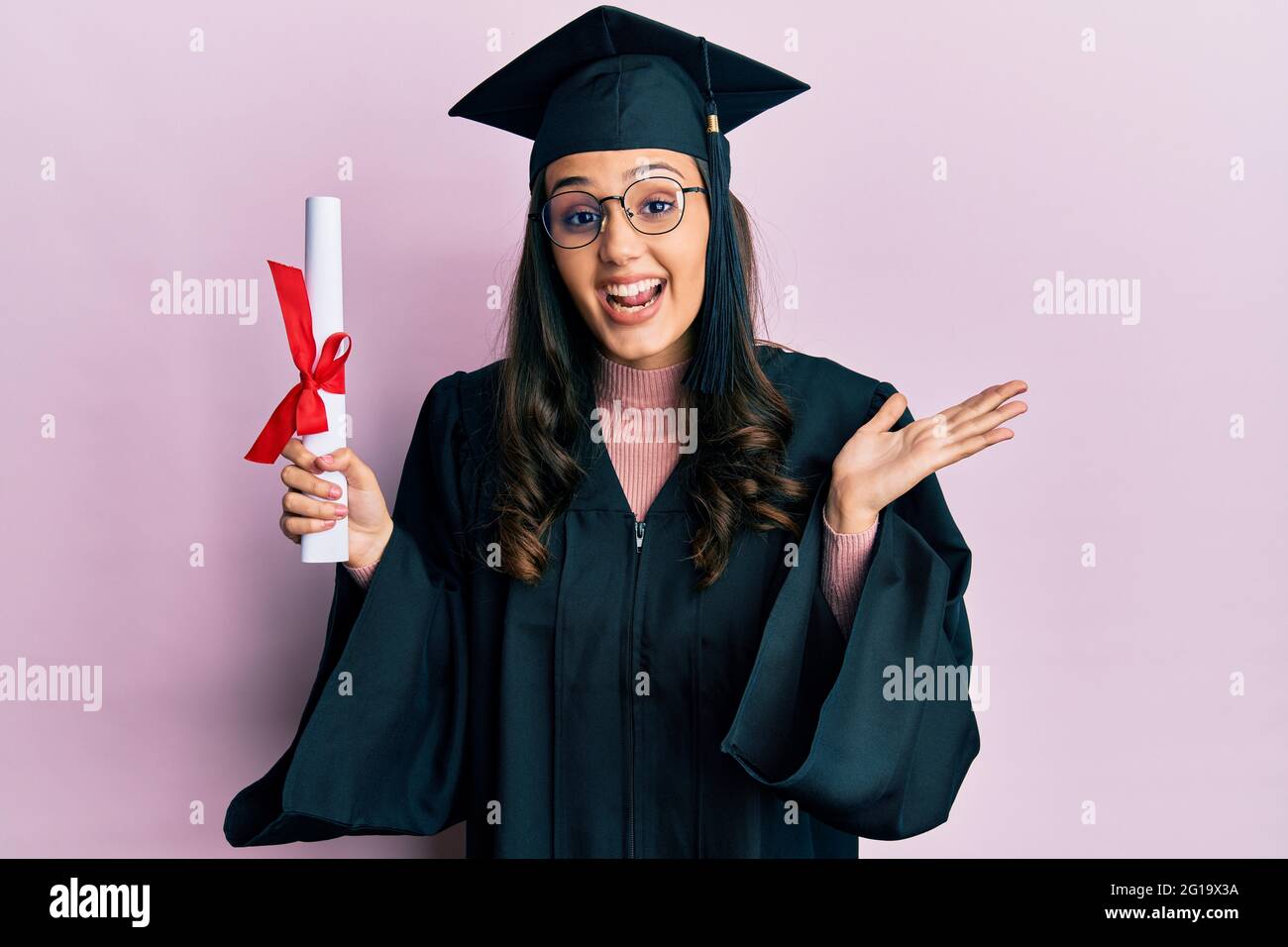 Young hispanic woman wearing graduation uniform holding diploma ...