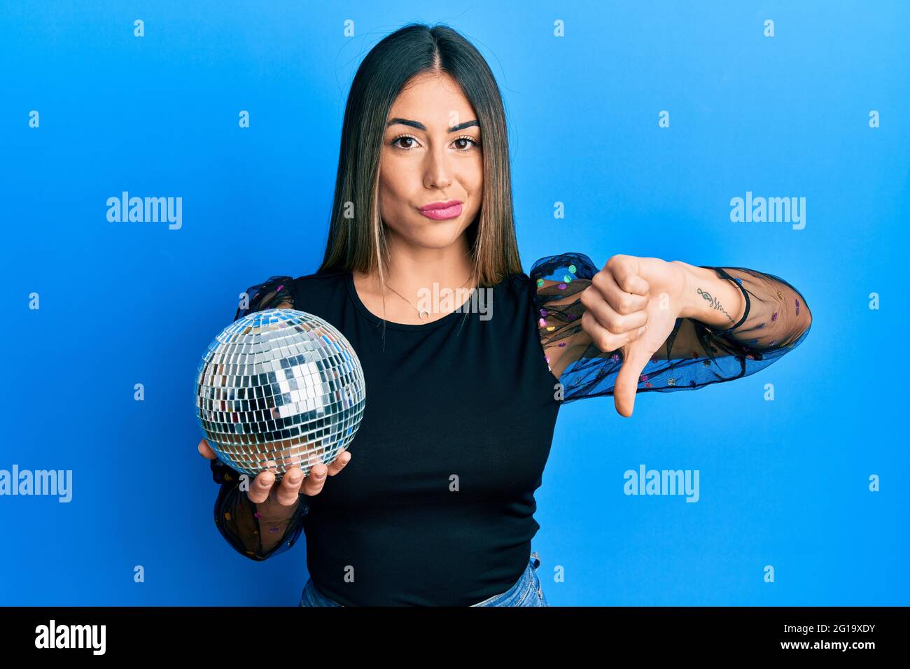 Young hispanic woman holding shiny disco ball with angry face, negative ...