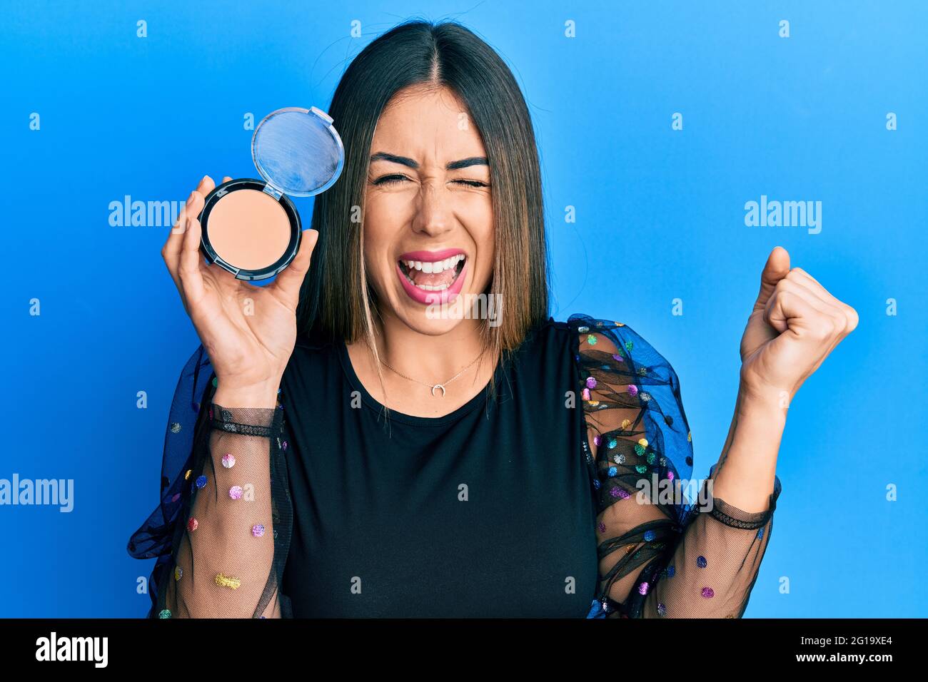 Young hispanic woman holding makeup powder screaming proud, celebrating ...