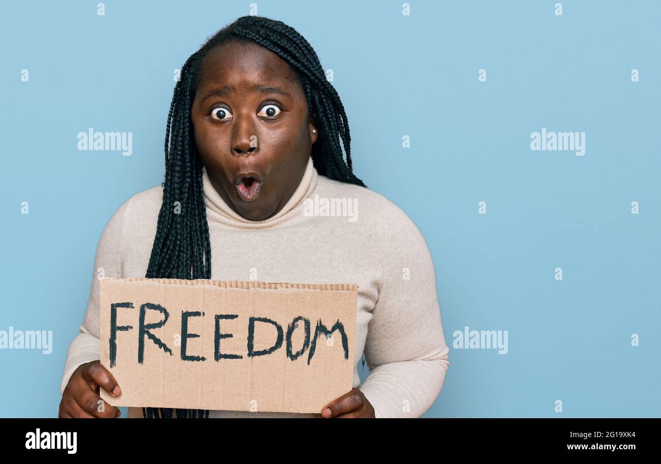 Young black woman with braids holding freedom banner scared and amazed ...