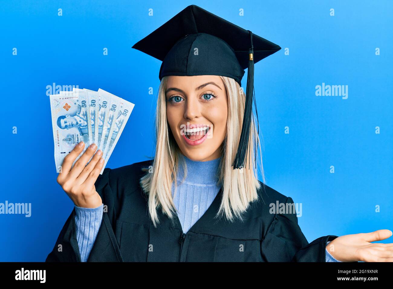 Beautiful blonde woman wearing graduation cap and ceremony robe holding ...