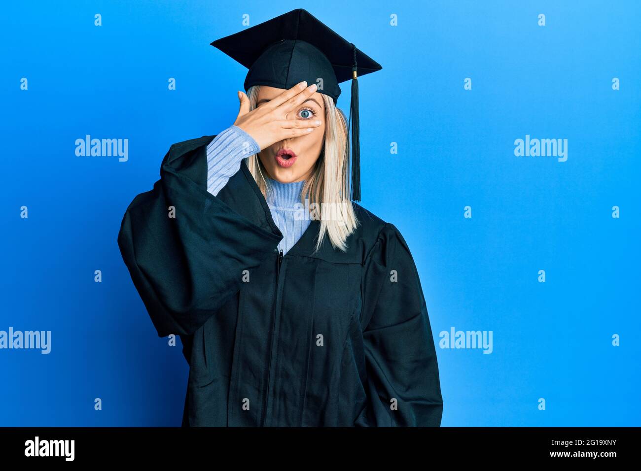 Beautiful blonde woman wearing graduation cap and ceremony robe peeking ...