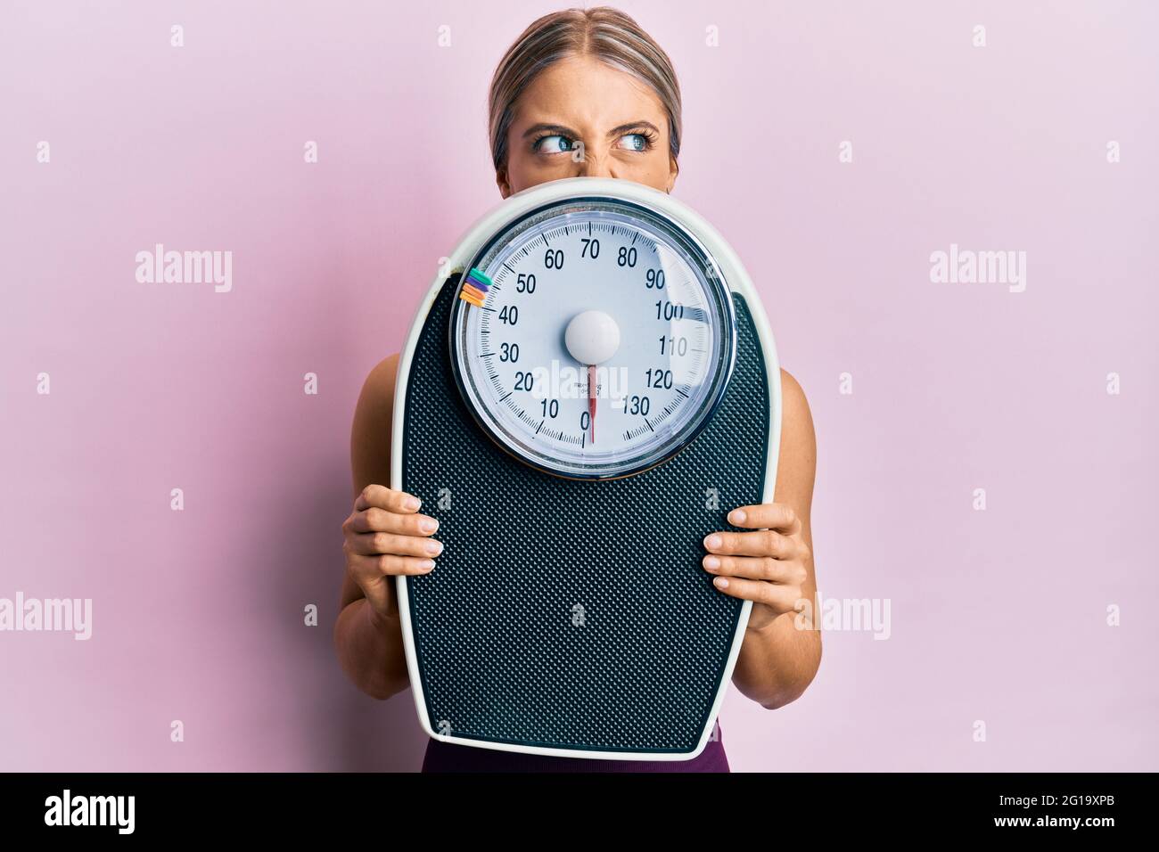 Beautiful blonde woman holding weight machine to balance weight loss ...